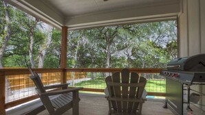 Uma área externa coberta com duas cadeiras Adirondack, uma churrasqueira e vista para uma área arborizada.