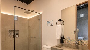 Uma casa de banho com chuveiro envolto em vidro, sanita, lavatório com espelho e barra de toalhas.