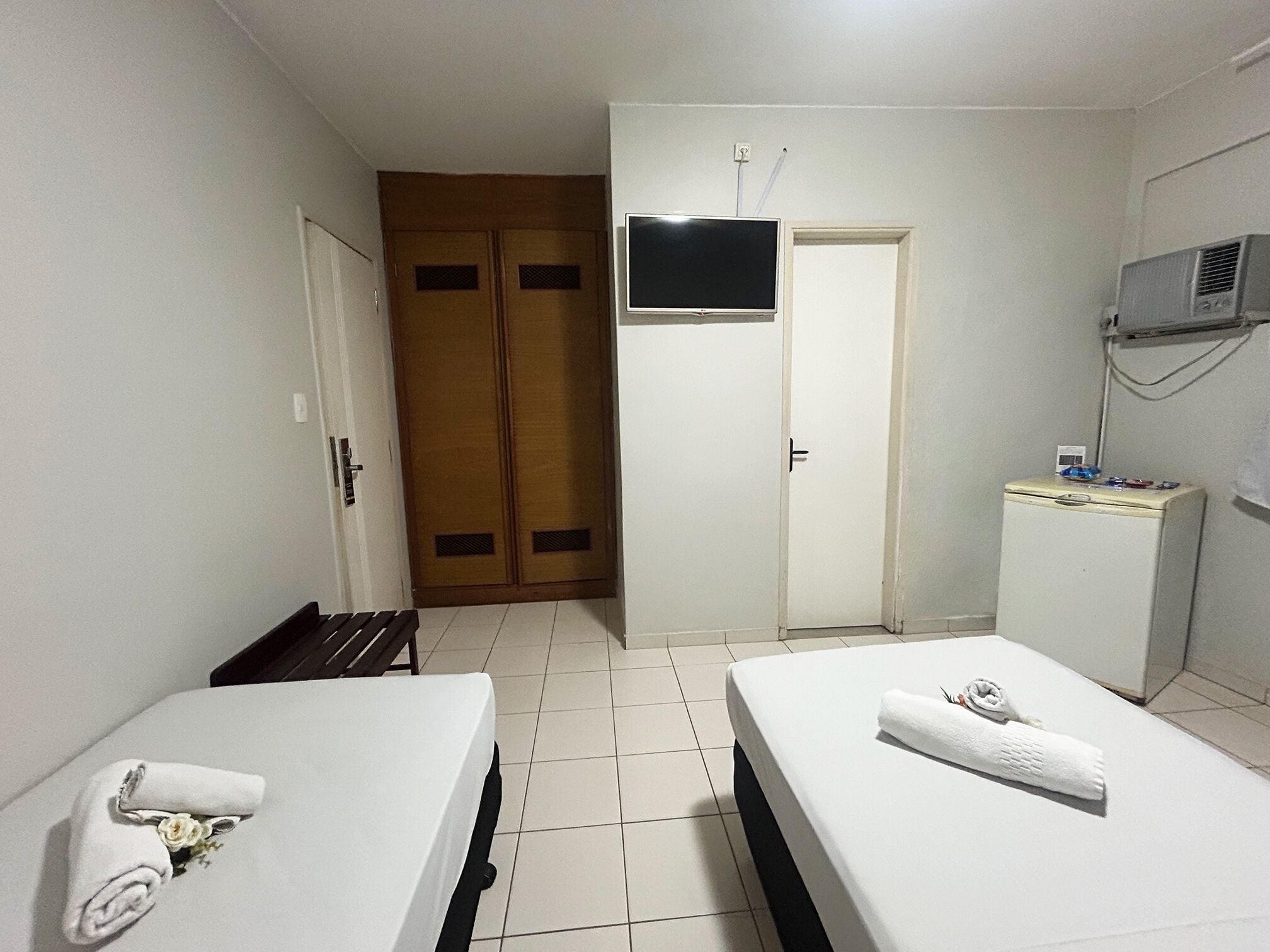 Quarto de hotel com duas camas, televisão, minibar e guarda-roupa.