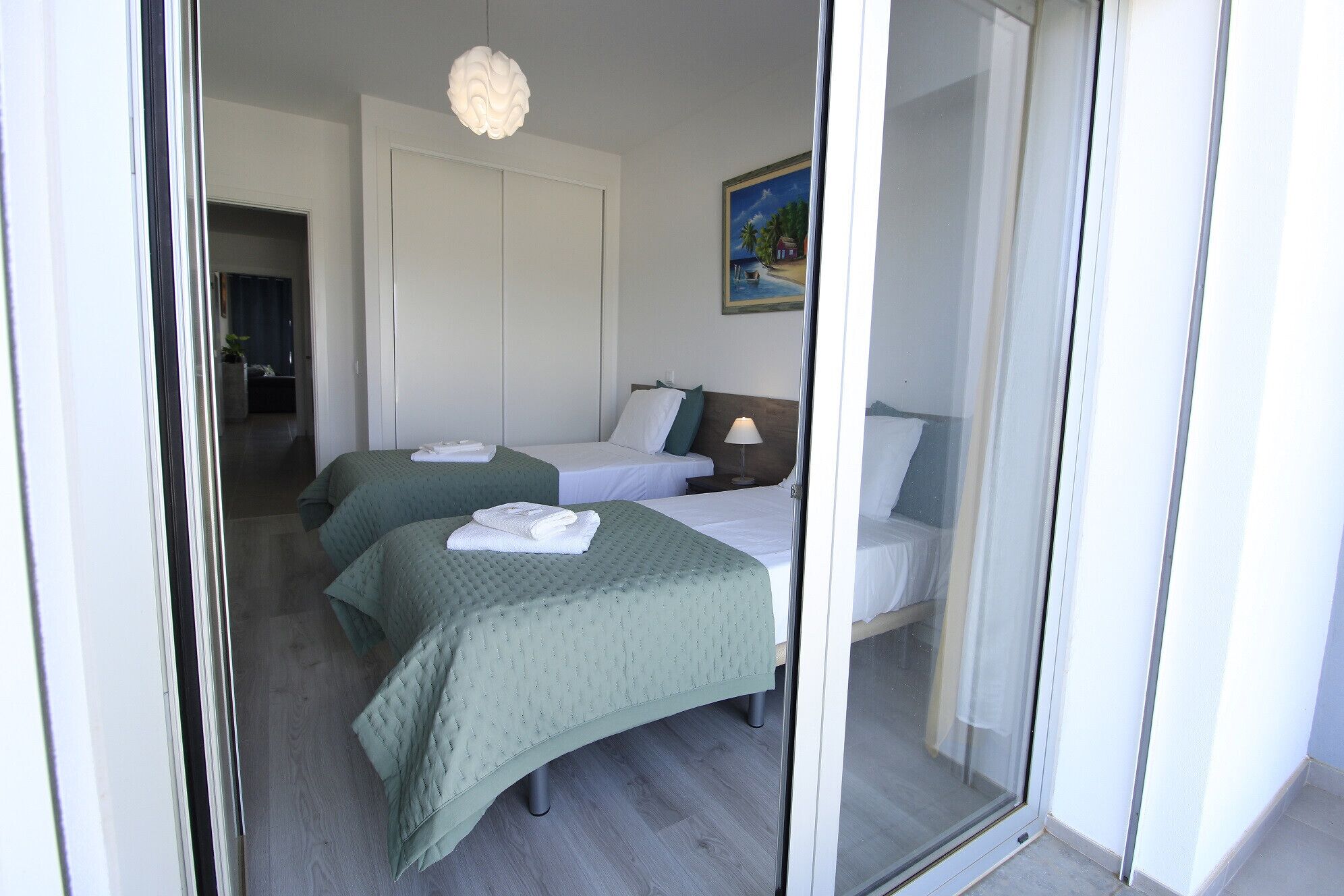 Quarto de hotel com duas camas, um quadro na parede e uma porta que dá para outro espaço.