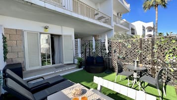 Um edifício de dois andares com varandas, um pátio com móveis para área externa e uma mesa posta com frutas e bebidas.
