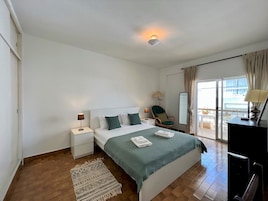 Quarto de hotel com cama, mesa de cabeceira, cadeira, espelho e varanda com vista.