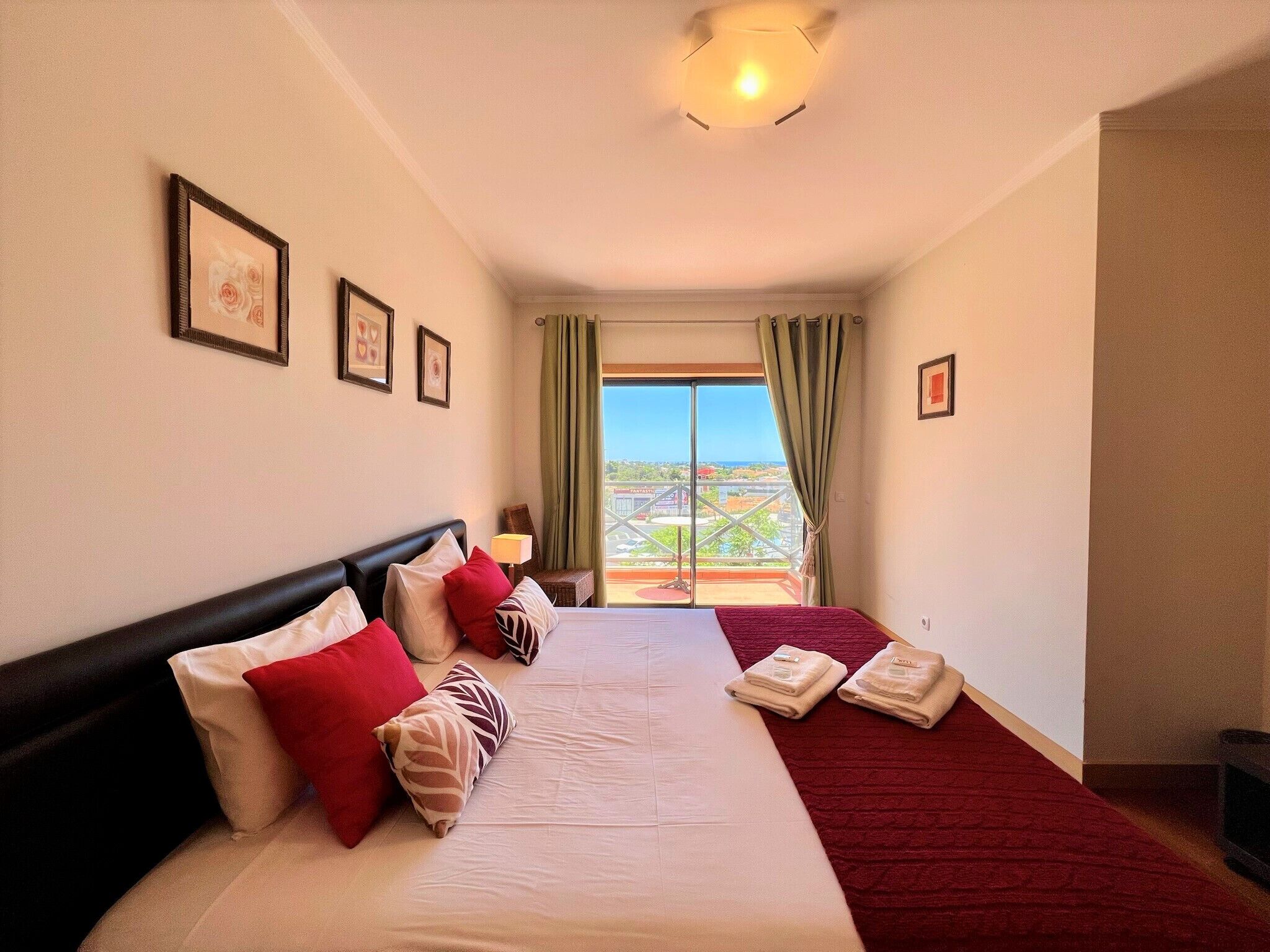 Quarto de hotel com uma cama grande, vista da cidade por uma varanda e uma luminária no teto.