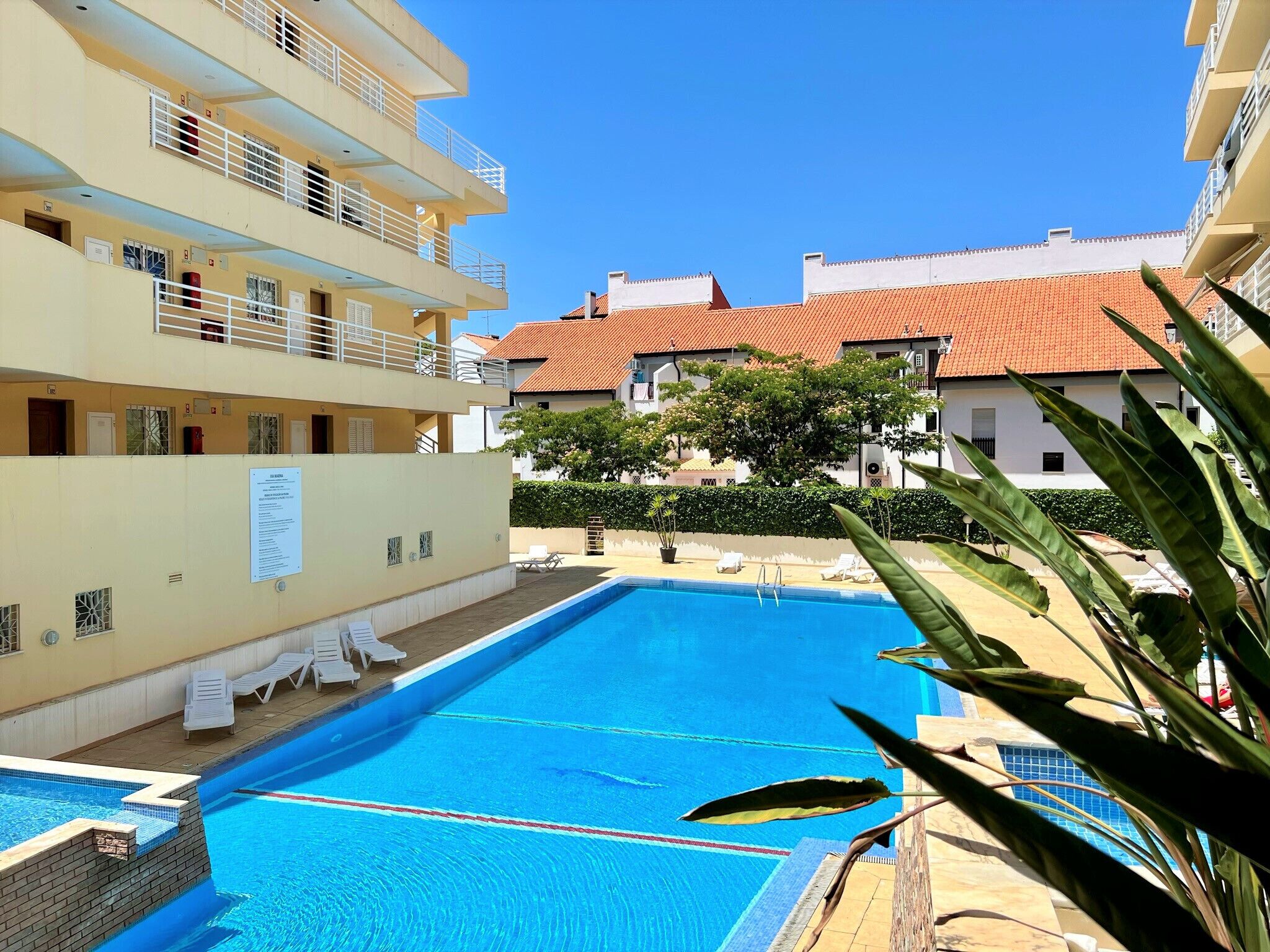 Piscina com espreguiçadeiras e vista para um prédio residencial com varandas.