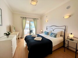 Quarto de hotel com cama, mesas de cabeceira, escrivaninha, cadeira e vista para a varanda.