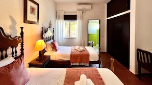 Quarto de hotel com duas camas, janela com cortinas, ar condicionado e vista para o exterior.