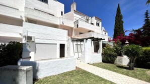 Um edifício branco com várias varandas, uma área externa coberta e um gramado bem cuidado.