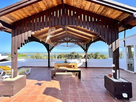 Uma área externa coberta com pérgola de madeira, uma mesa e cadeiras.