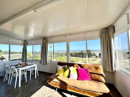 Um quarto iluminado pelo sol, com uma janela grande, um sofá e uma mesa de jantar.