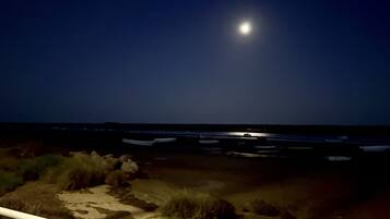 Cena noturna da praia com barcos e uma lua.