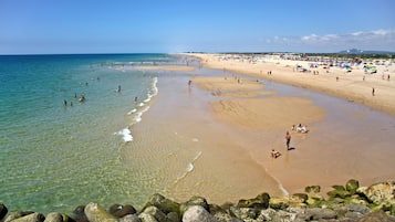 Uma praia com água cristalina, areal arenoso e rochas em primeiro plano.