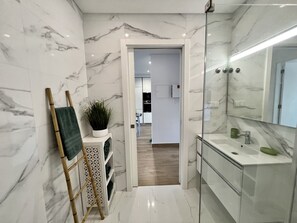 Uma casa de banho moderna com um espelho grande, paredes de mármore e zona de duche.