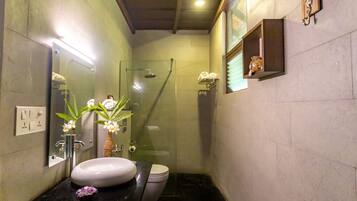 Uma casa de banho com uma pia branca, sanita, cabine de duche em vidro e espelho com luz acima.