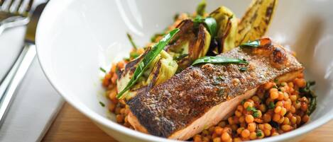 Uma tigela branca com salmão grelhado, legumes assados e lentilhas.