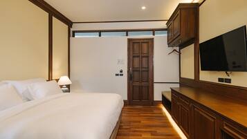 Quarto de hotel com uma cama grande, piso de madeira, televisão fixada na parede e guarda-roupa de madeira.