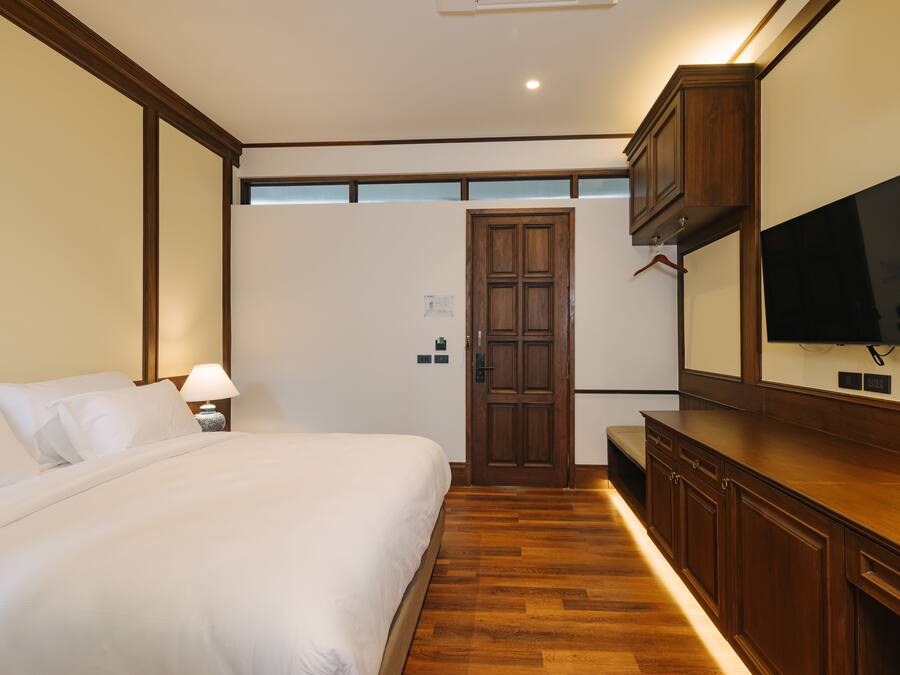 Quarto de hotel com uma cama grande, piso de madeira, televisão fixada na parede e guarda-roupa de madeira.