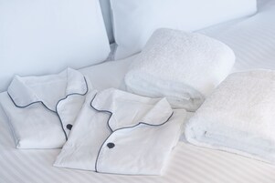 Almofadas brancas e fronhas a jogo, dobradas sobre uma cama com padrão listrado.