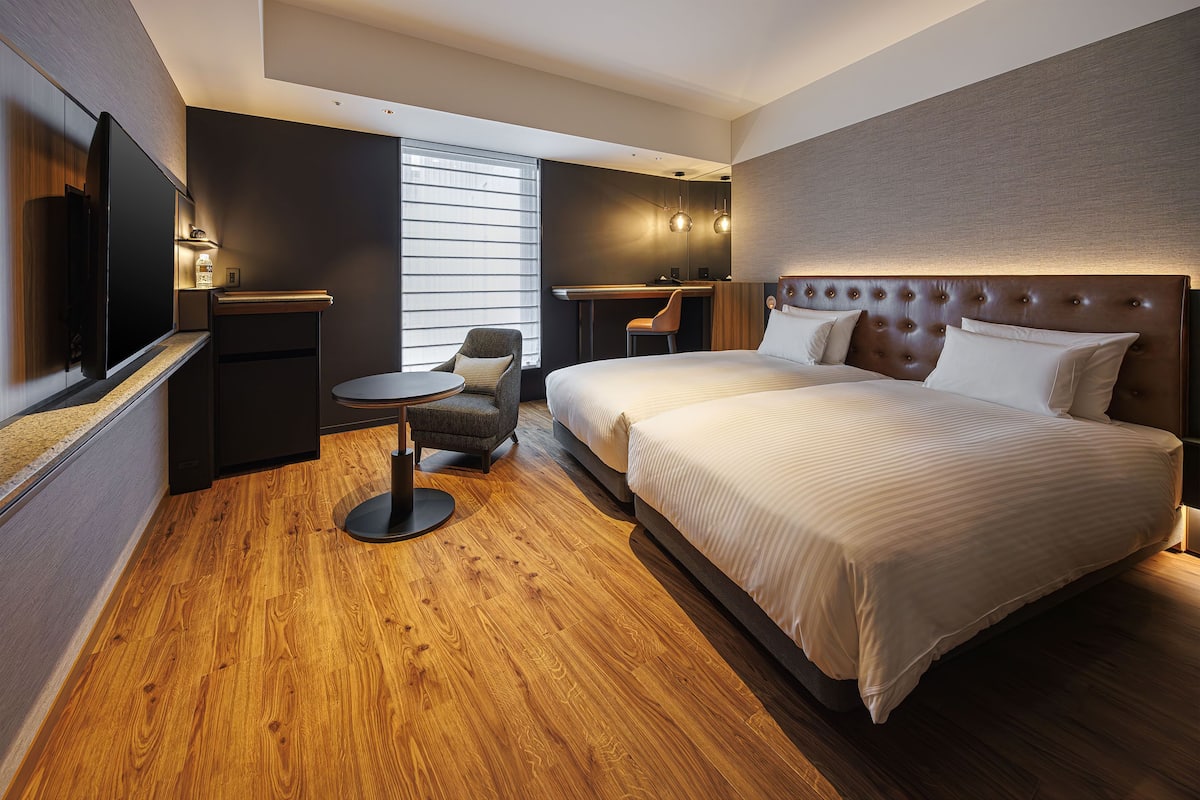 Quarto de hotel com uma cama grande, uma escrivaninha, uma cadeira e uma televisão.
