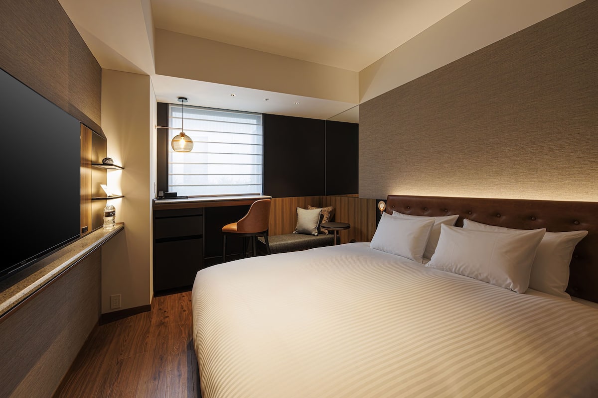 Quarto de hotel moderno com uma cama grande, uma escrivaninha e um espaço de estar confortável.