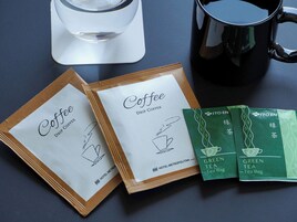Dois sacos de café, um copo de água e uma caneca preta sobre uma mesa.