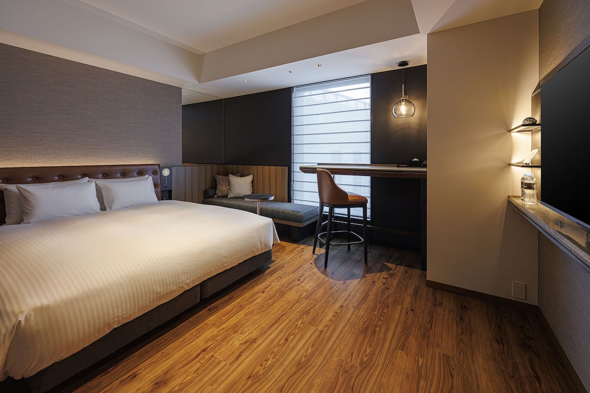 Quarto de hotel moderno com uma cama grande, uma mesa e uma cadeira.