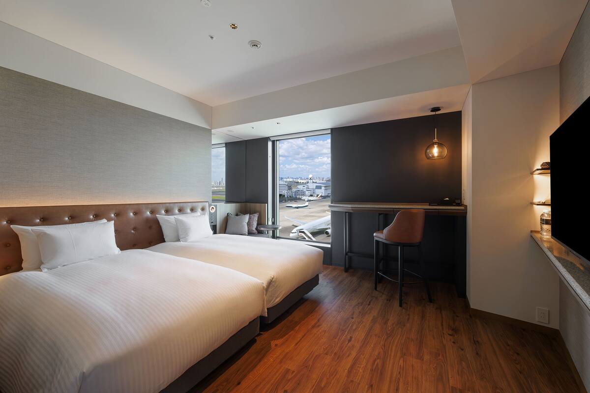 Quarto de hotel moderno com uma cama grande, uma escrivaninha e vista para a cidade.