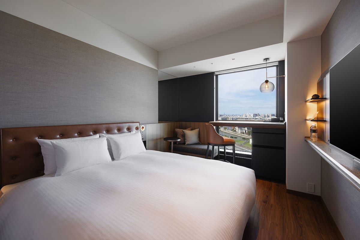 Quarto de hotel moderno com uma cama grande, área de estar com vista e janela com vista para a cidade.