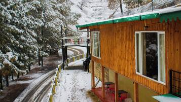 Uma cabana de madeira com varanda coberta, um espaço de estar ao ar livre e vista para uma paisagem coberta de neve.
