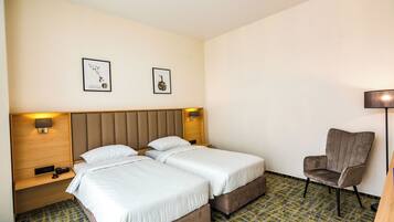 Quarto de hotel com duas camas, uma cadeira, um abajur e obras de arte na parede.