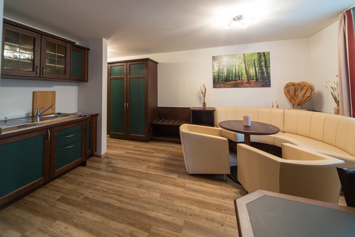 Um espaço compacto com cozinha compacta, um sofá, uma pequena mesa e uma pintura de uma paisagem florestal.
