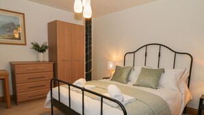 Quarto bem arrumado com cama, guarda-roupa de madeira, mesa de cabeceira e abajur.