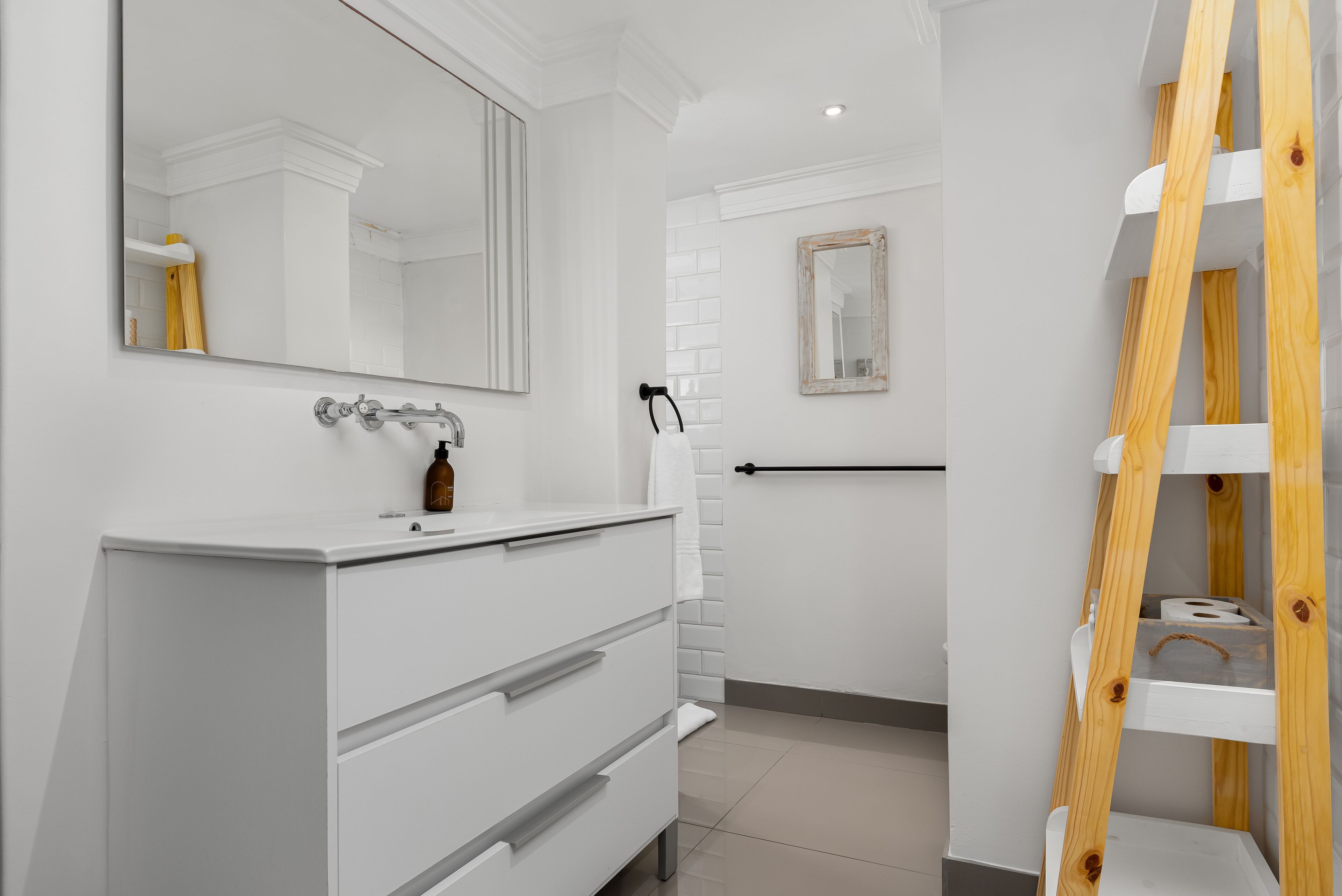 Uma casa de banho moderna com uma toucador branco, um espelho grande e uma escada de madeira.