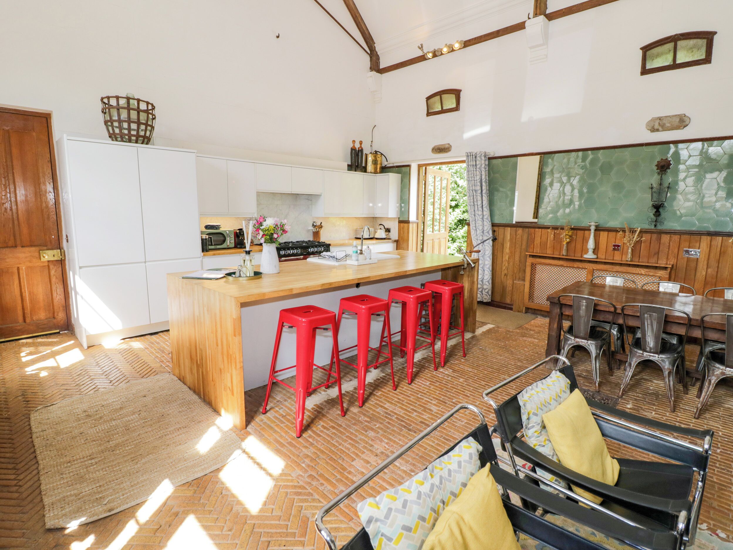 Uma cozinha espaçosa com uma ilha central, banquetas vermelhas e um espaço de refeições com mesa e cadeiras.