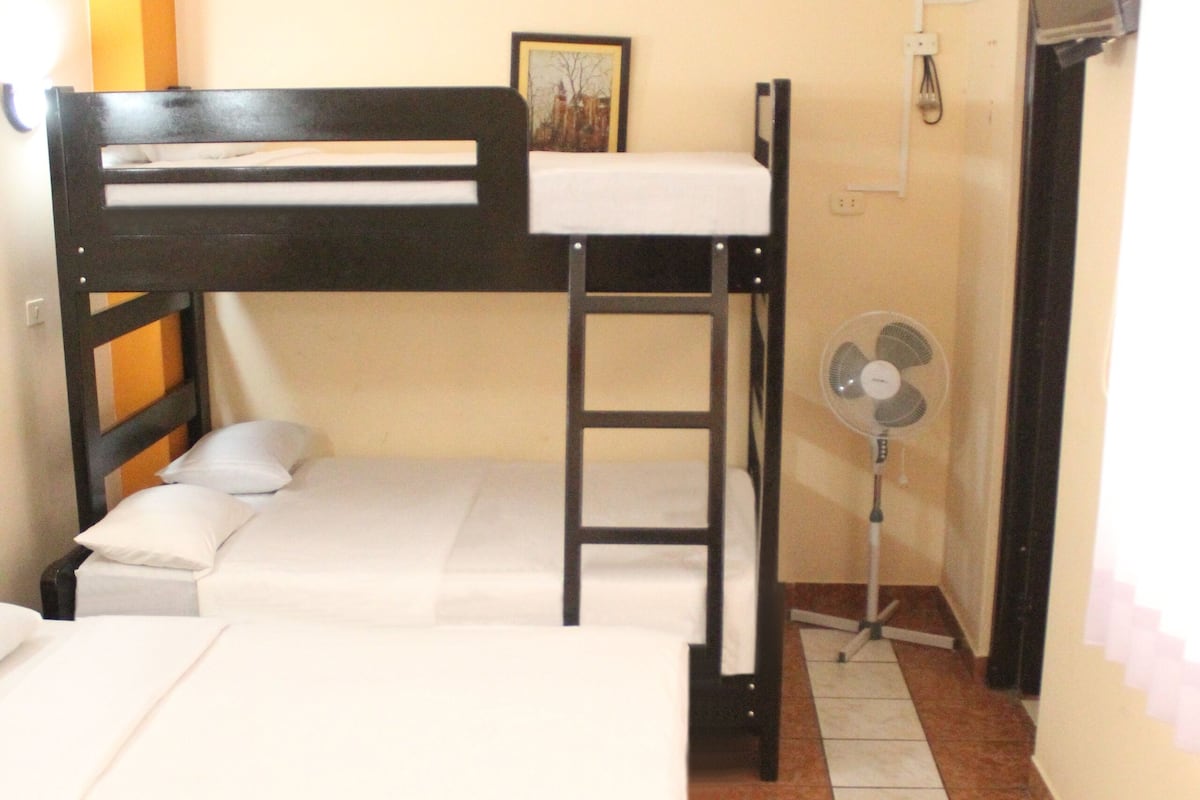 Quarto com beliche, ventoinha no teto e televisão na parede.