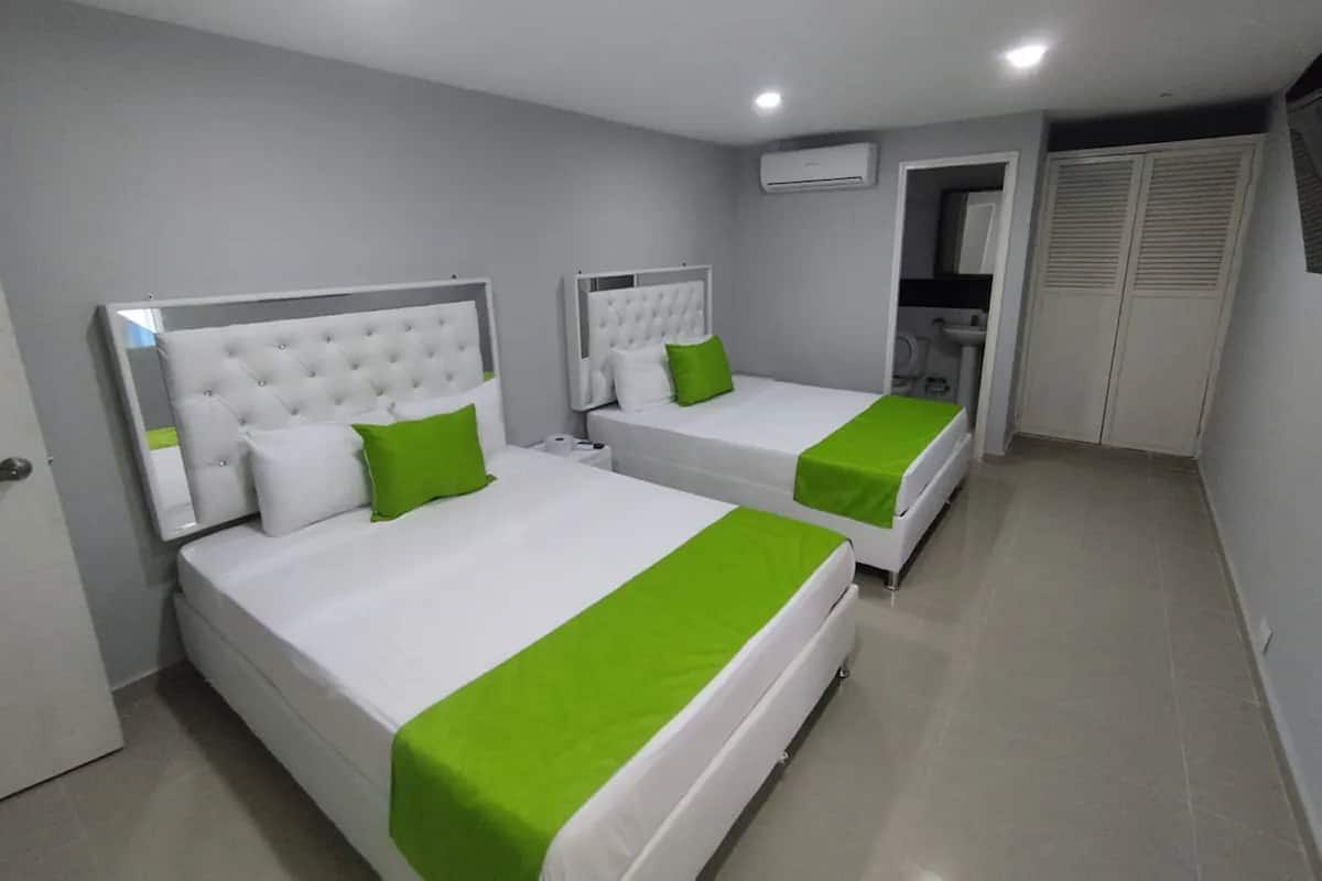 Quarto de hotel com duas camas, cada uma com cabeceira branca e cobertores verdes.