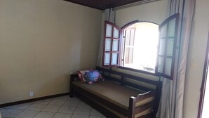 Um quarto com um banco de madeira, uma janela com persianas de madeira e piso de azulejos.