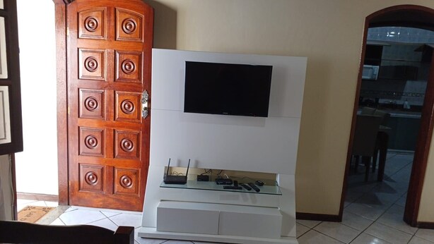Uma sala de estar com um rack branco, uma televisão de tela plana e uma porta de madeira com painéis decorativos.