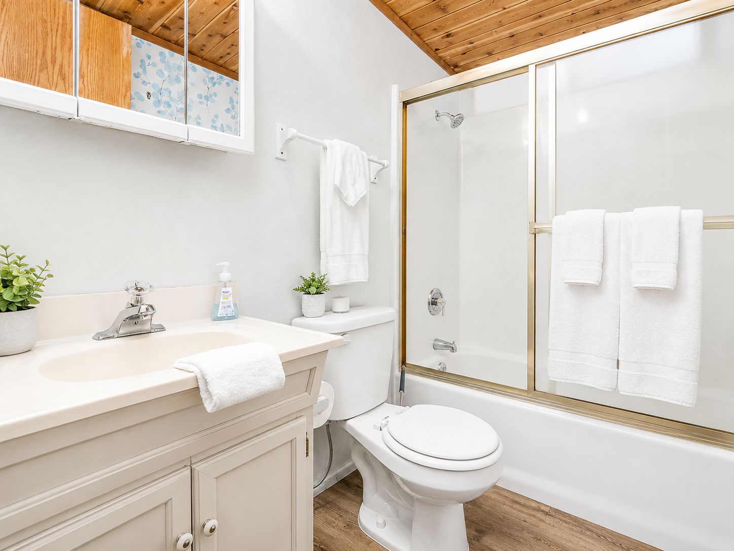 Casa de banho com lavatório branco, sanita e banheira. Existem cabines de duche com paredes de vidro e moldura dourada.
