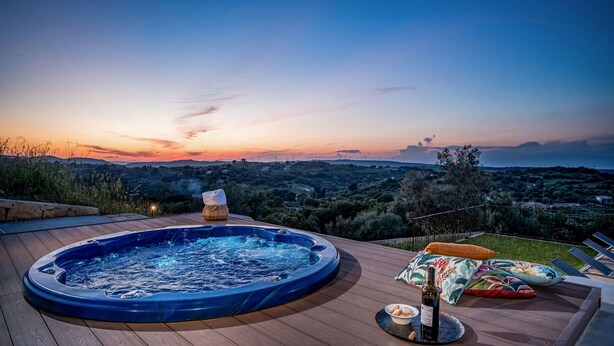 Uma banheira de hidromassagem em deck de madeira com vista para um pôr do sol cênico.