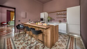 Cozinha compacta com ilha de madeira, banquetas, frigorífico e área de refeições com chão estampado.