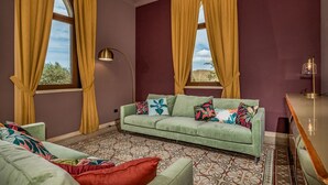 Quarto com sofá verde, tapete estampado e vista através de janelas amplas.