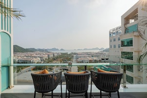 Uma varanda com duas cadeiras e uma mesa, com vista para um horizonte costeiro com edifícios e colinas.