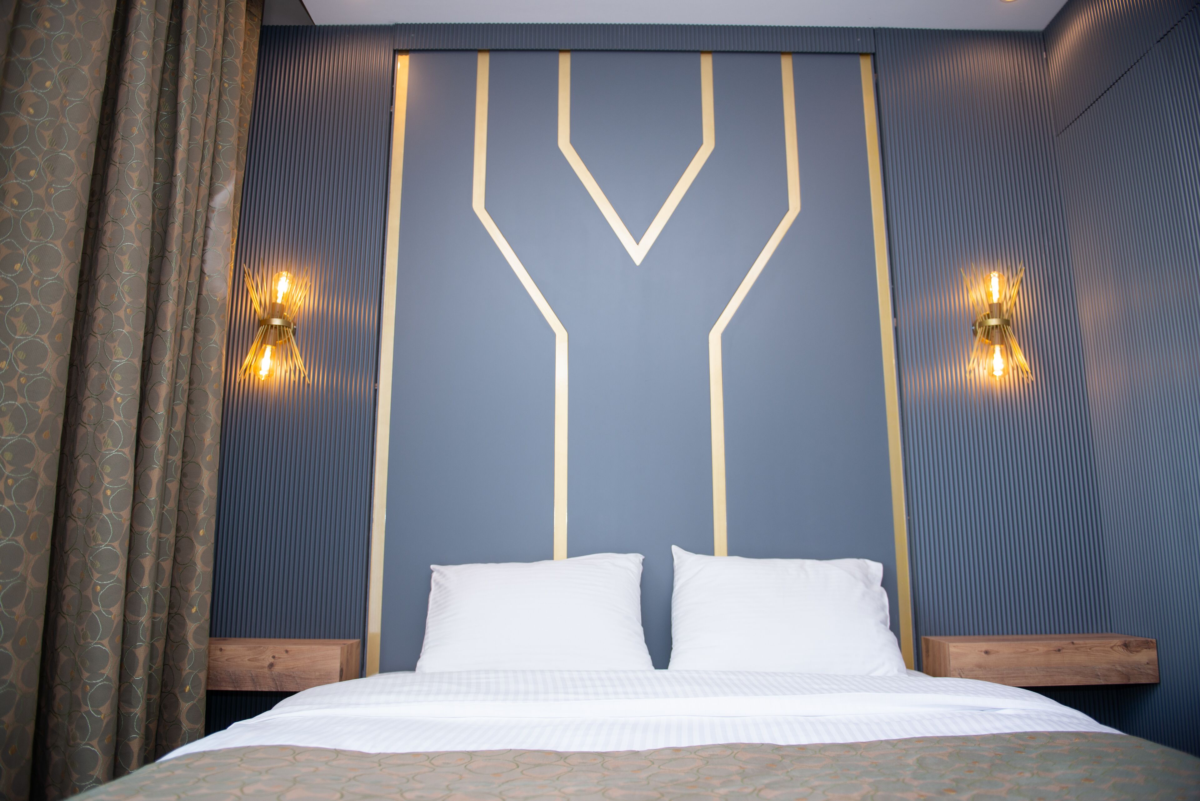 Cama bem arrumada com lençóis brancos em quarto com parede azul e luminárias decorativas.