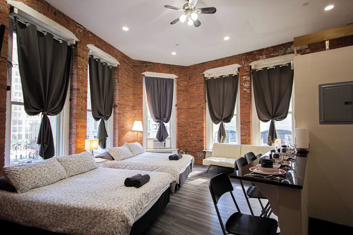 Quarto de hotel com duas camas, uma mesa, uma cadeira e uma janela com cortinas.