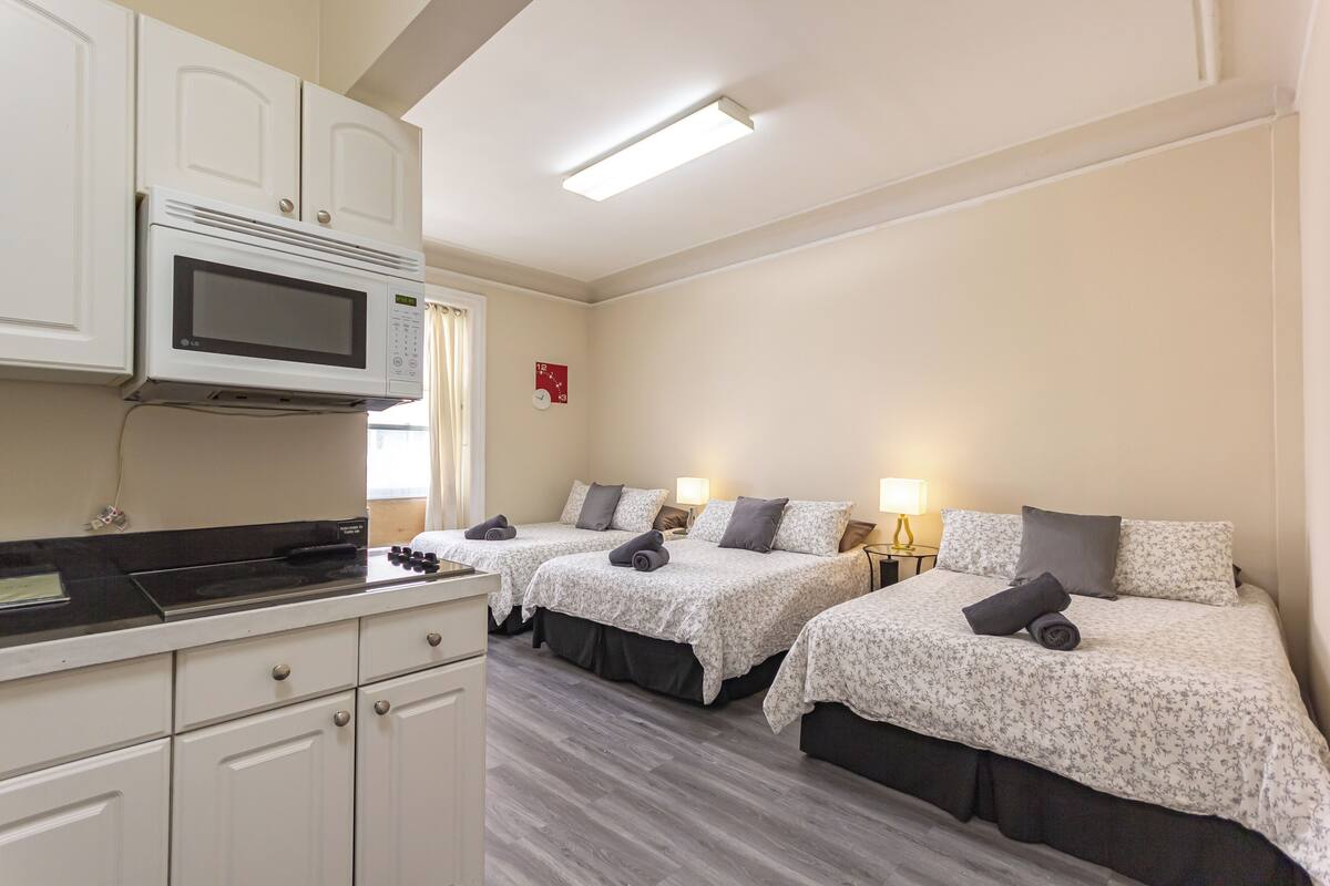 Quarto de hotel com duas camas, uma cozinha compacta e micro-ondas.
