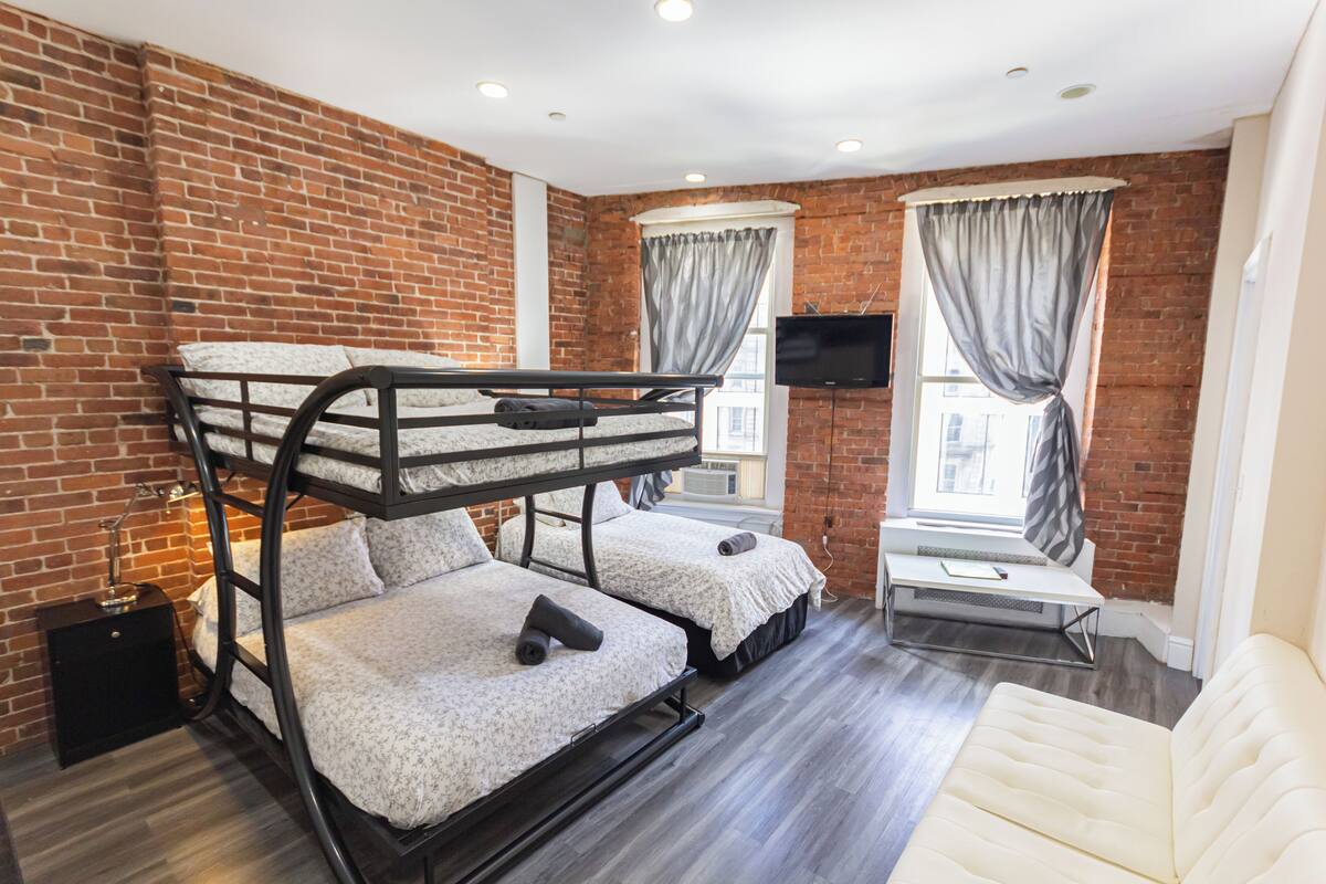Um quarto com beliches, televisão de tela plana, janela com cortinas e um sofá.