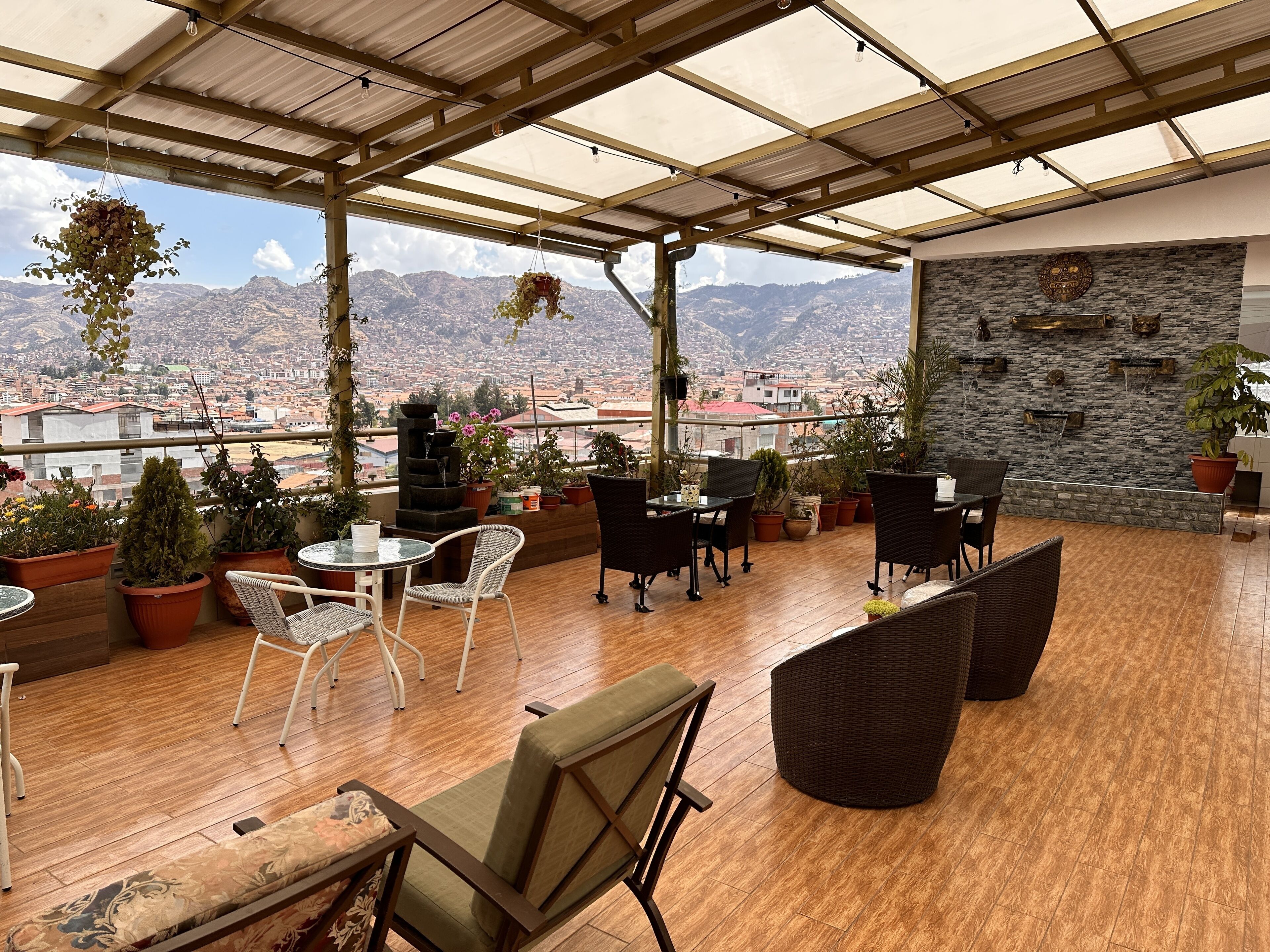 Uma área de estar coberta ao ar livre, com piso de madeira, móveis de vime e plantas em vasos.