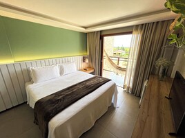 Quarto de hotel com cama, mesa de cabeceira, luminária, televisão e vista para o exterior.