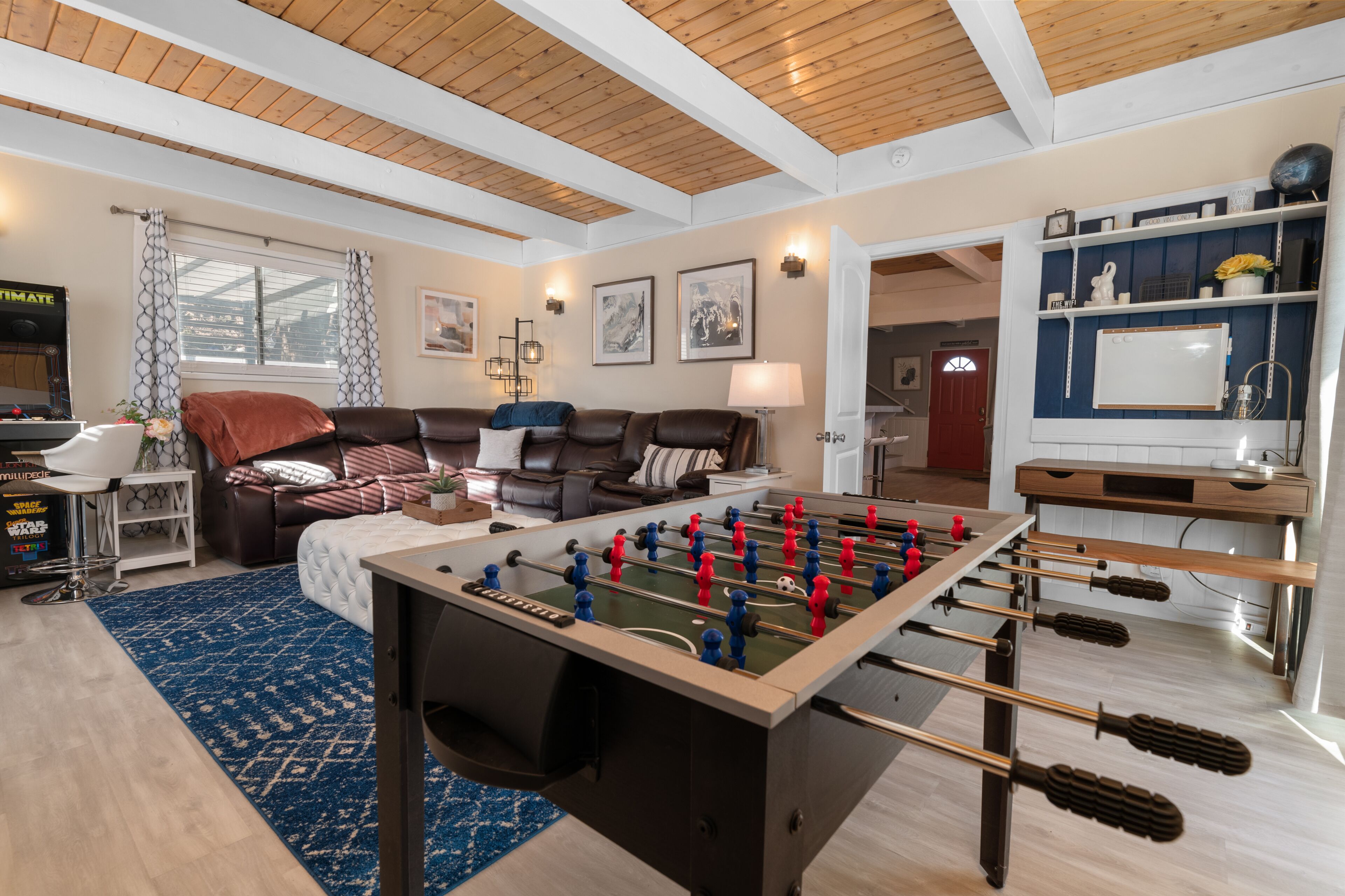 Uma sala de estar acolhedora com mesa de futebol, assentos confortáveis e uma área de cozinha com prateleiras.