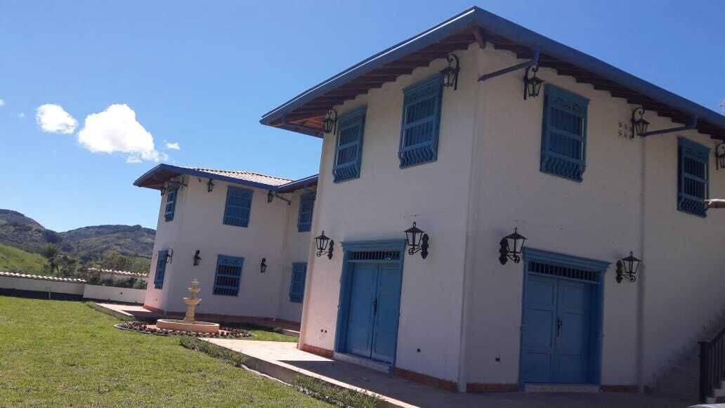 Um edifício de dois andares com fachada branca e detalhes azuis, apresentando uma entrada central com porta azul e uma pequena fonte na frente.